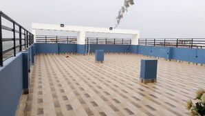 Um terraço no telhado com piso xadrez, grades azuis e vista para a paisagem urbana.