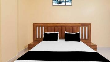 Quarto com cabeceira de madeira, duas almofadas pretas e colcha branca.