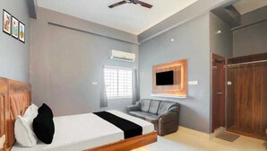 Quarto com cama, sofá cinza, televisão na parede e guarda-roupa de madeira.