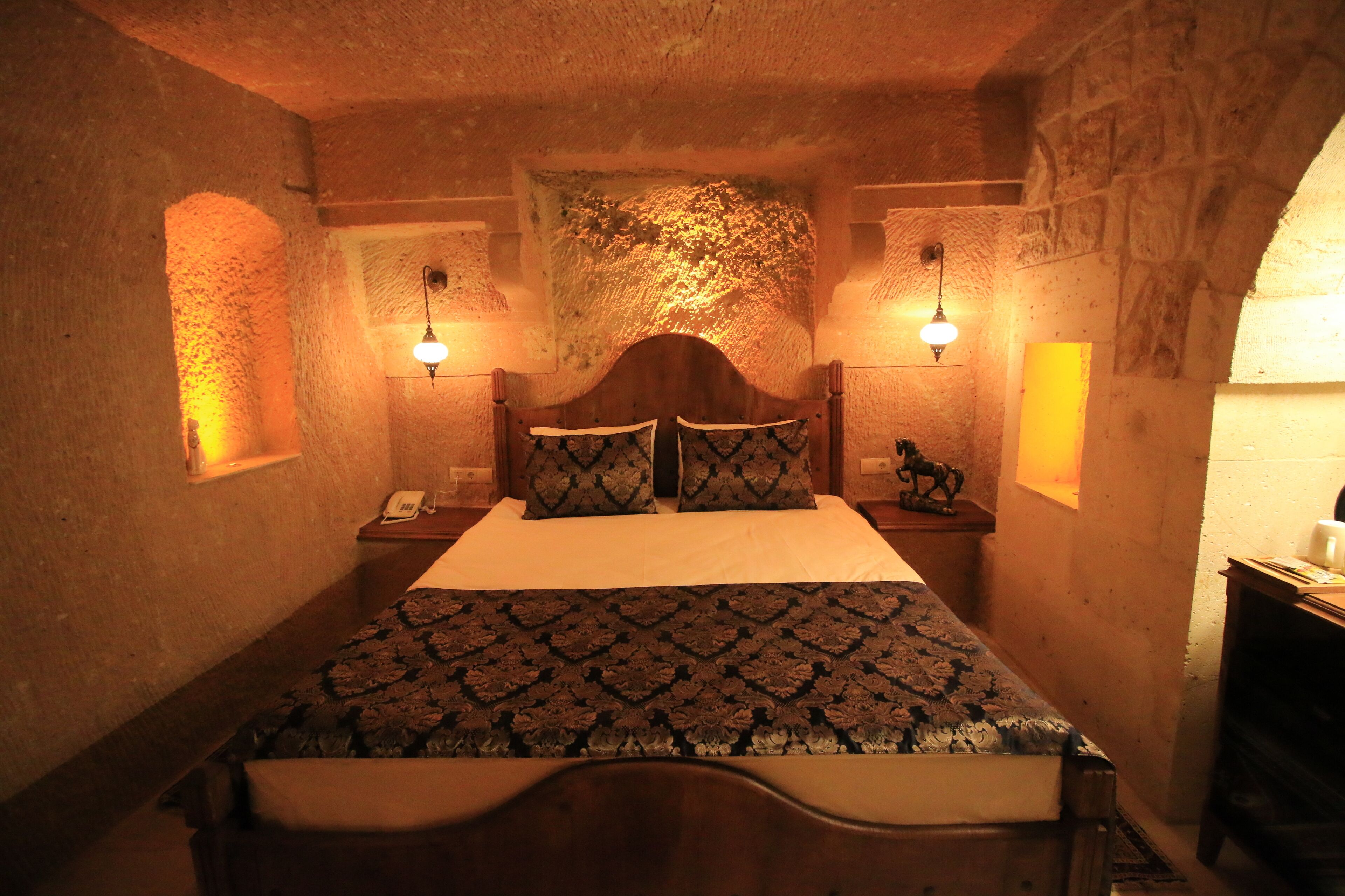 Quarto com uma cama grande, duas mesas de cabeceira e uma luminária fixada na parede.