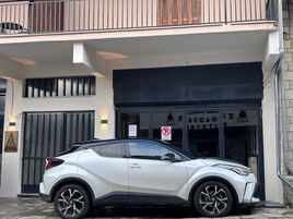 Um SUV branco estacionado em frente a um edifício com placa de 'Proibido Estacionar', entrada com portão e varanda com grade.