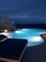 Uma área à beira da piscina com espreguiçadeiras, piscina e vista para o mar.
