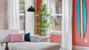 Quarto com sofá branco, luminária de chão preta, planta de bambu e uma prancha de surf na parede.