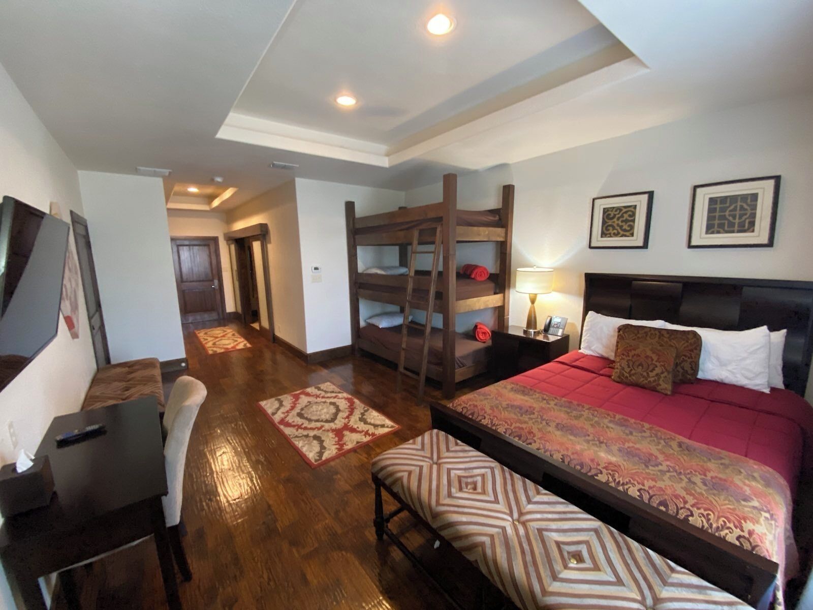 Quarto de hotel com beliches, uma escrivaninha, uma cadeira, cama com colcha estampada e mesa de cabeceira com abajur.