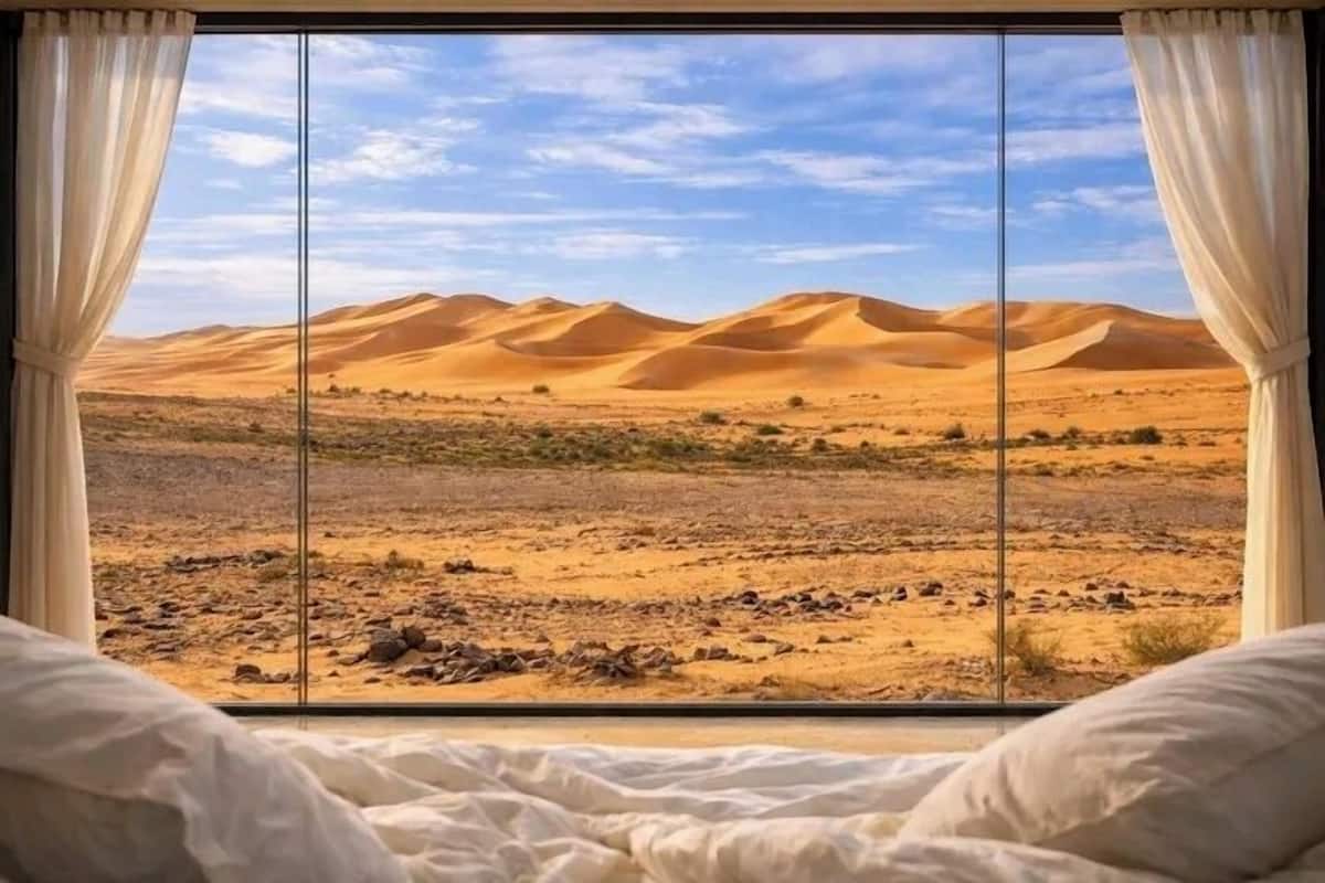 Quarto com uma grande janela que oferece vista para dunas de areia.