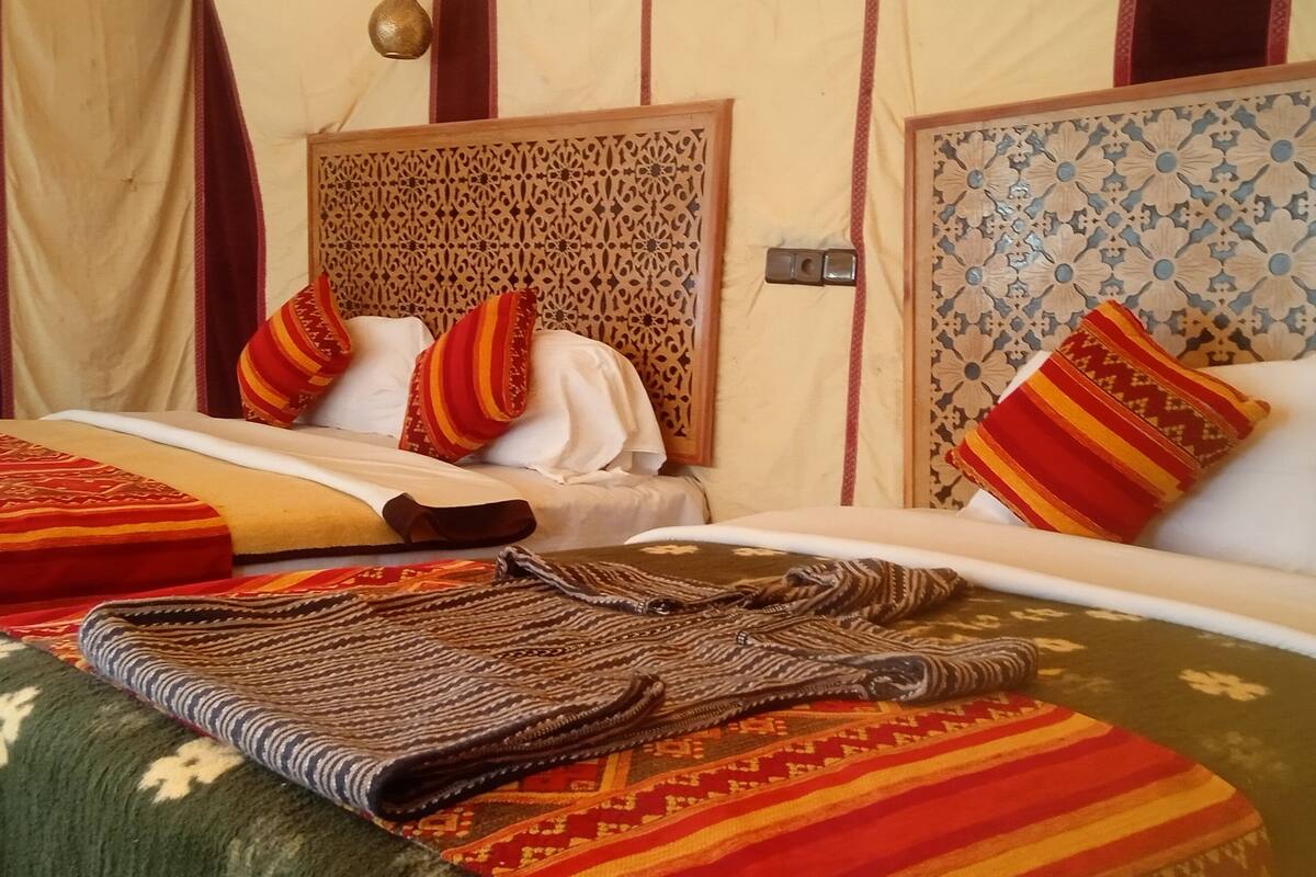 Quarto de hotel com duas camas, cada uma com roupa de cama e almofadas estampadas.