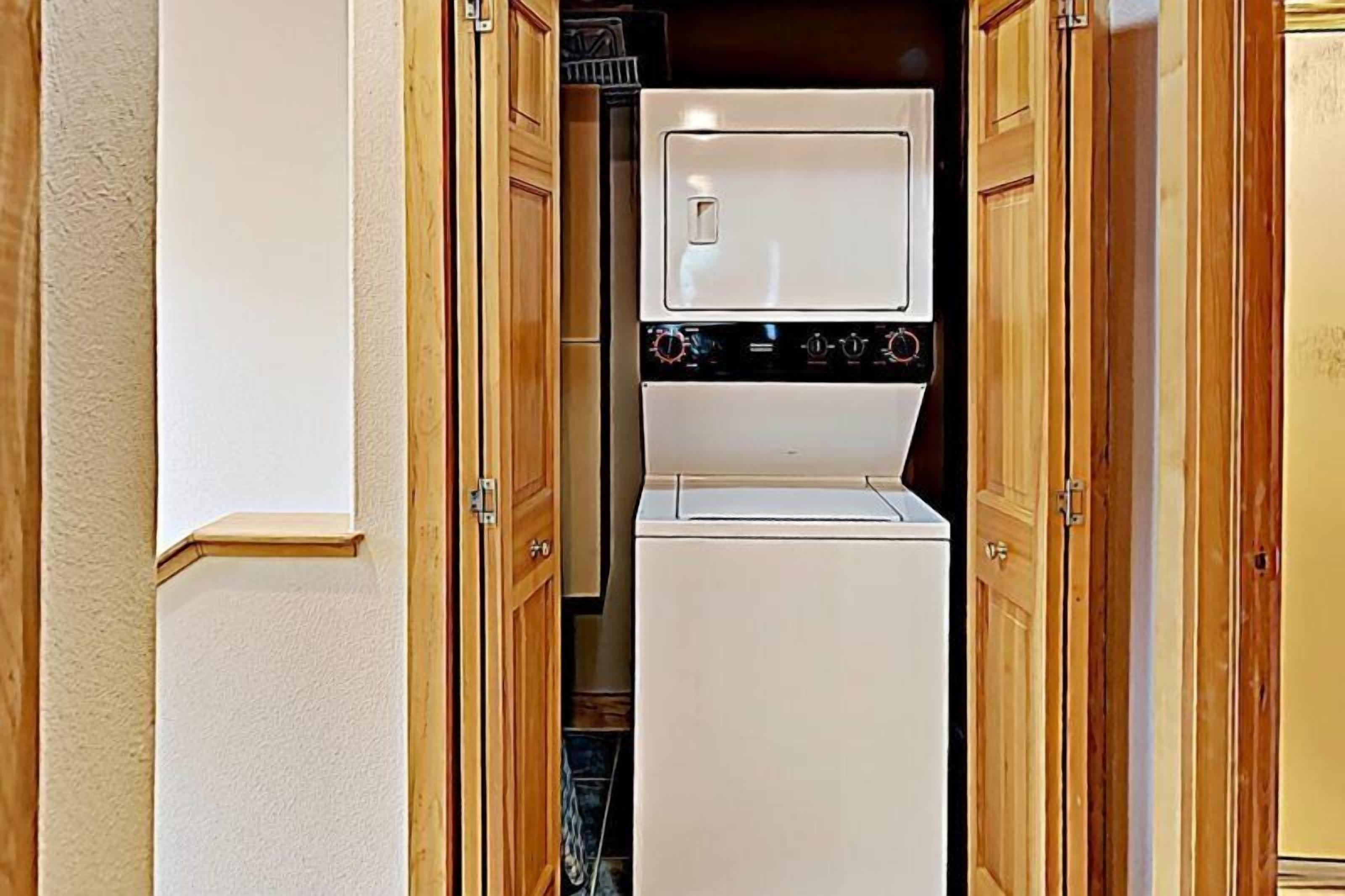 Uma cozinha compacta com forno embutido e micro-ondas, armários de madeira e um frigorífico pequeno.