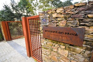 Um muro de pedra com um portão de metal e uma placa com o texto 'MOINHOS DO PAIVA COUNTRY HOUSE'.