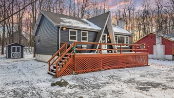 Uma casa com varanda coberta, um galinheiro pequeno e um celeiro vermelho em uma paisagem nevada.