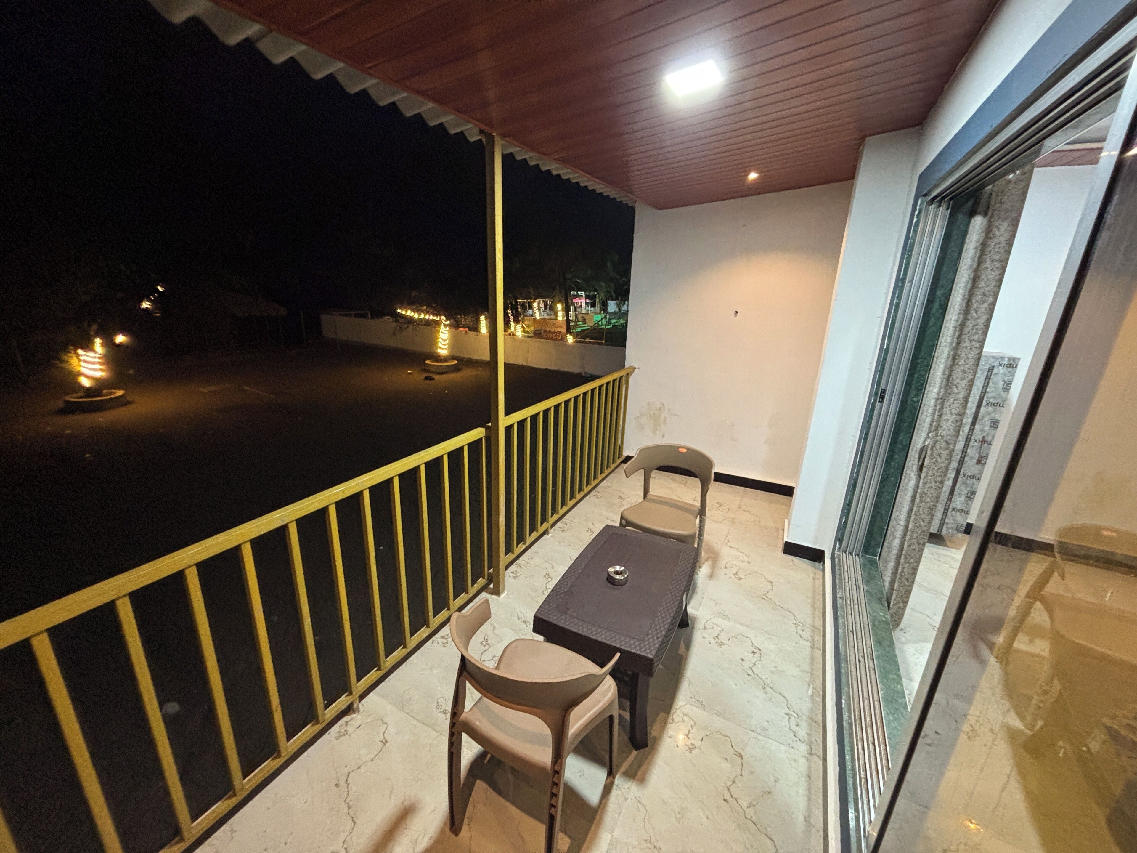 Varanda com mesa e cadeiras, corrimão e vista da rua à noite.