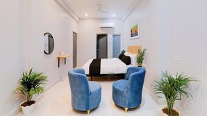 Quarto de hotel moderno com uma cama, duas poltronas azuis e plantas em vasos.