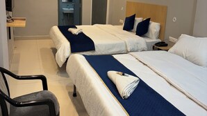 Quarto de hotel com duas camas, uma escrivaninha, uma cadeira, uma televisão e um aparelho de ar condicionado.