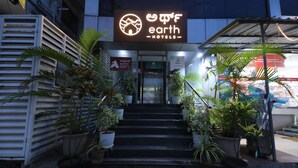 Entrada de hotel com uma placa indicando "earth hotels", cercada por plantas em vasos e uma escadaria.