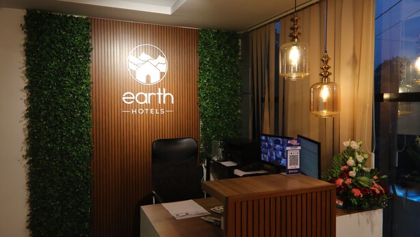 Balcão de recepção com um logotipo, uma cadeira de escritório preta, um monitor de computador e um arranjo floral.