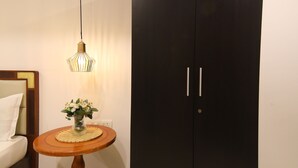 Um quarto com uma cama, uma mesa de madeira redonda com um vaso, um candeeiro pendente e um guarda-roupa preto.
