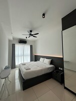 Quarto de hotel moderno com uma cama grande, um ventilador de teto, uma mesa de cabeceira, uma cadeira e um espelho amplo.