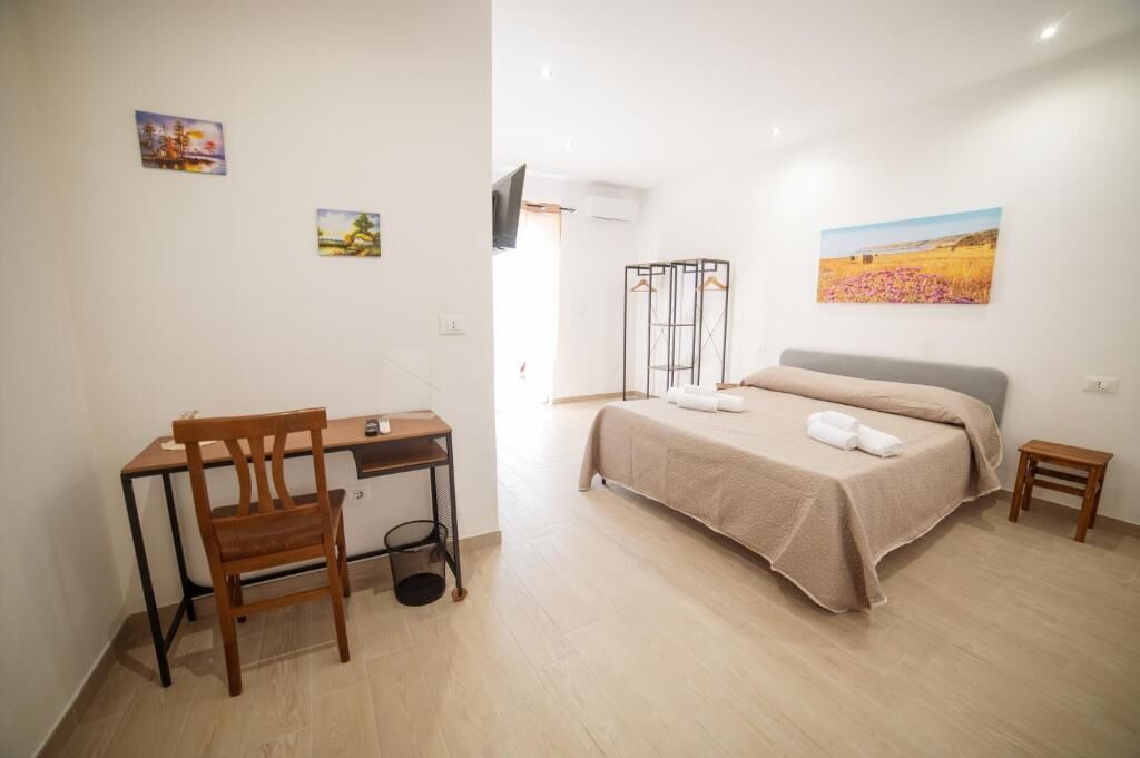 Quarto com cama, escrivaninha e cadeira. Há quadros nas paredes.