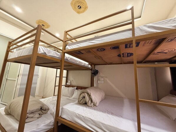 Quarto com beliche de madeira, roupa de cama branca e luminária no teto.