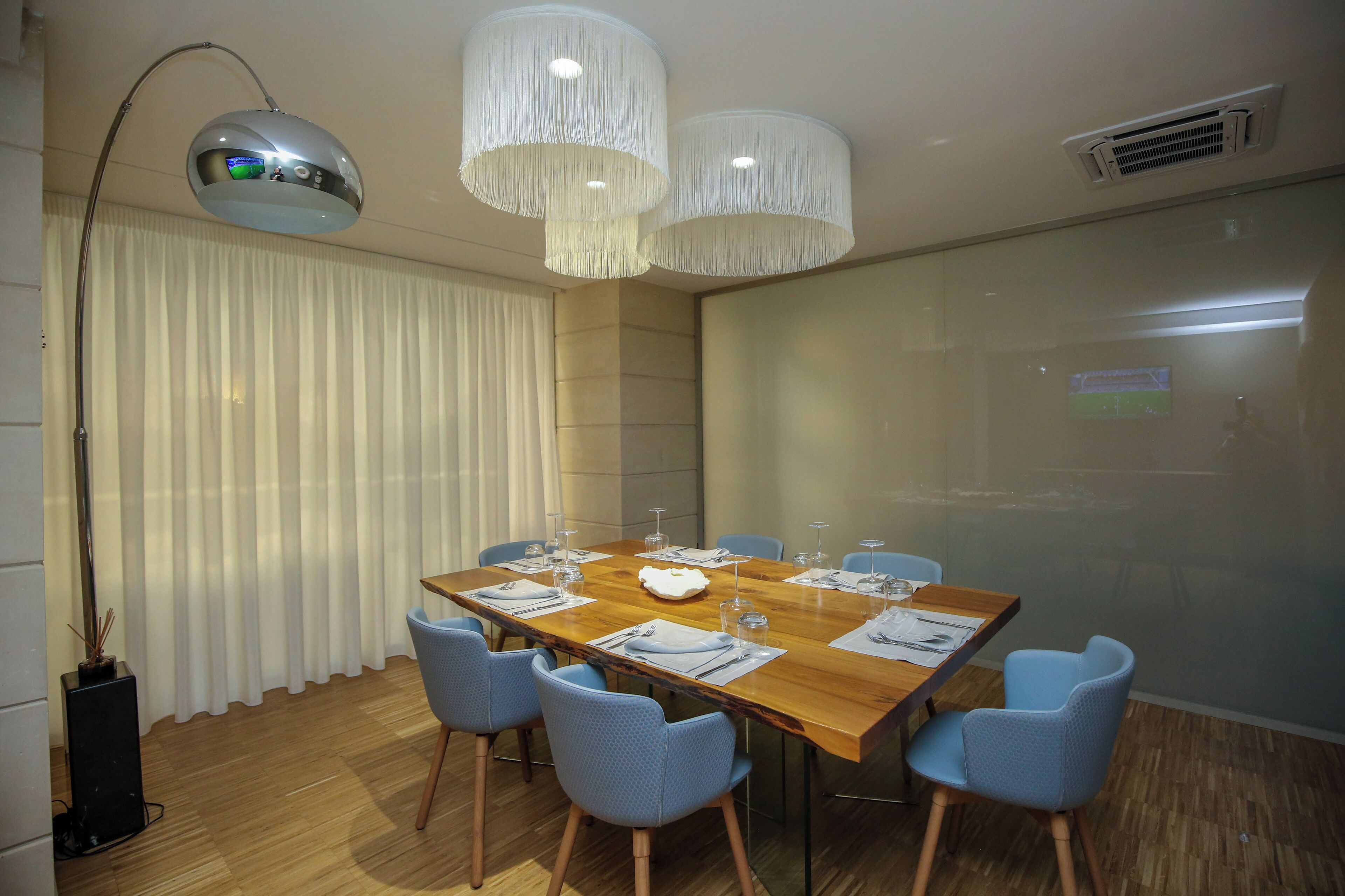 Uma sala de conferências com uma mesa de madeira, cadeiras azuis e um lustre moderno.