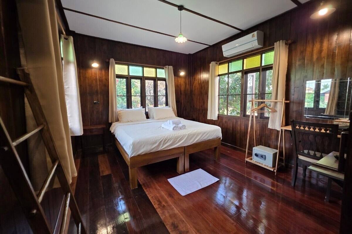 Quarto com piso de madeira, uma cama, mesa de cabeceira, luminária pendente e janela com cortinas.