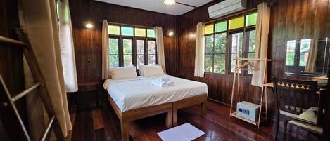 Quarto com piso de madeira, uma cama, mesa de cabeceira, luminária pendente e janela com cortinas.