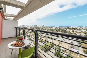 Varanda com mesa posta para o café da manhã, com vista para a paisagem urbana com edifícios e céu claro.