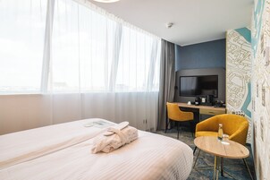 Quarto de hotel com cama, escrivaninha, televisão e uma mesinha.