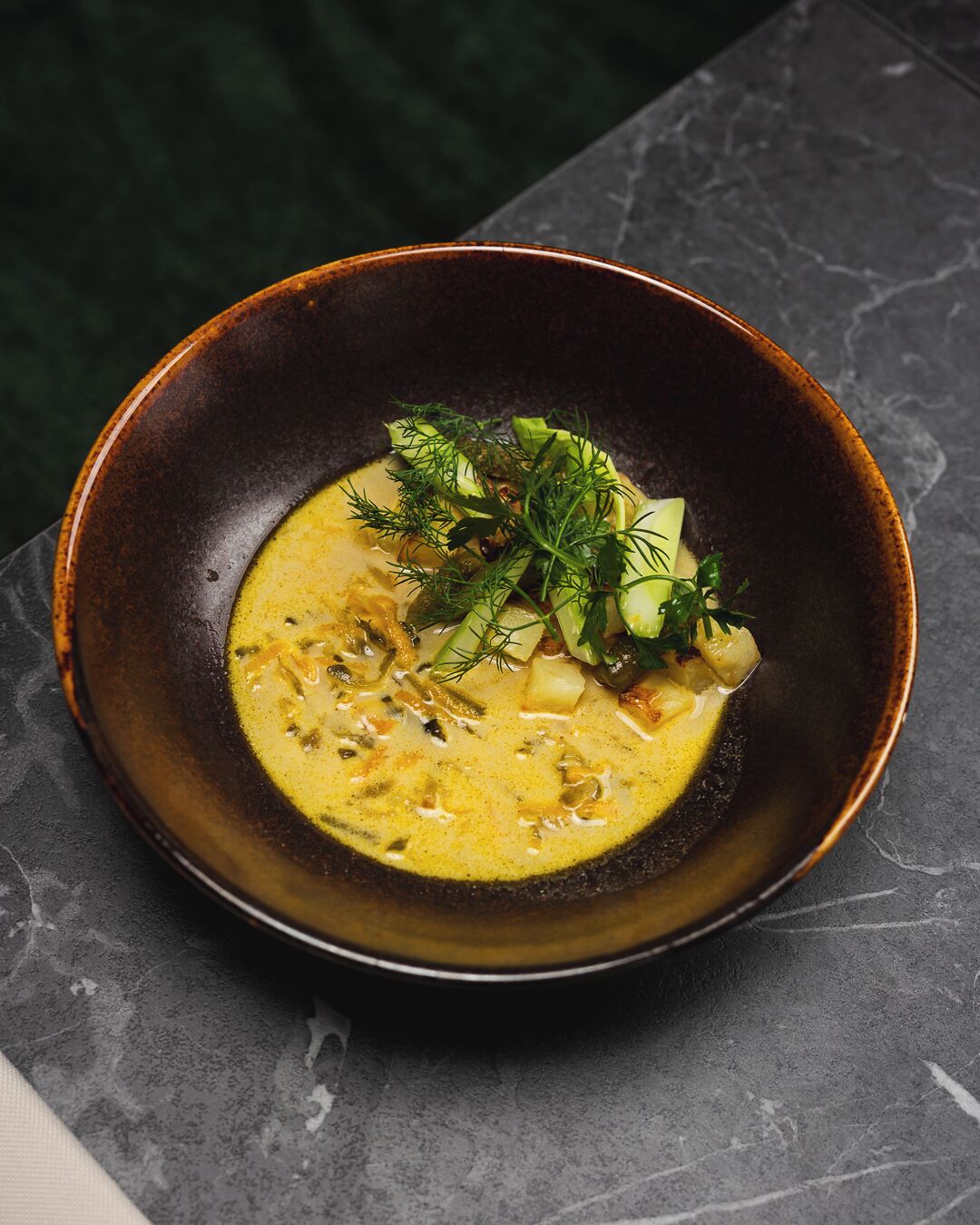 Uma tigela de sopa com vegetais e ervas sobre uma superfície escura.