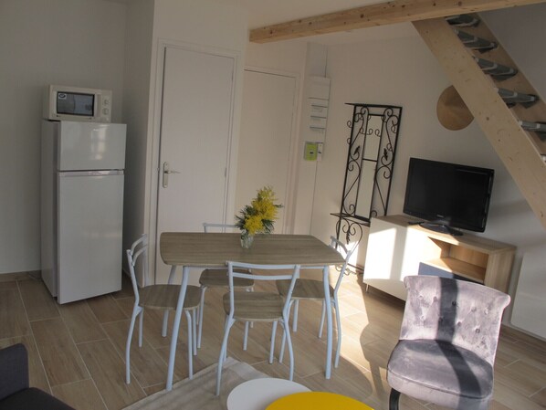 Um espaço de estar compacto com cozinha compacta, área de jantar com mesa e cadeiras, televisão em um suporte e uma escada.