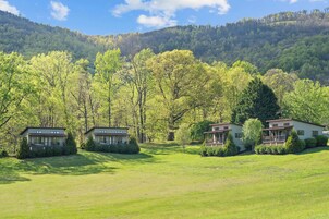 Um espaço com três cabanas, cada uma com varanda e cercada por vegetação exuberante e árvores.
