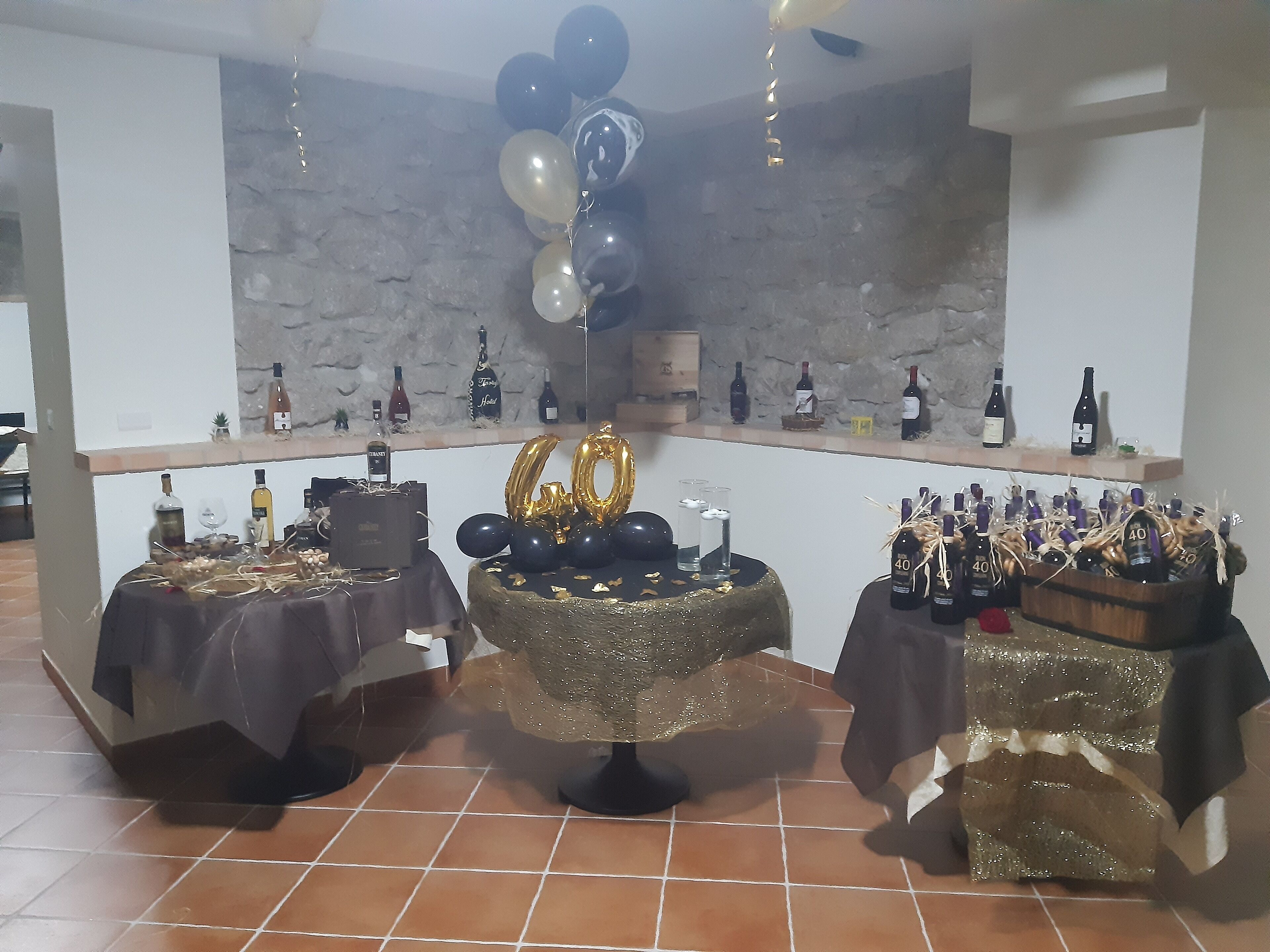 Quarto com parede de pedra, piso de azulejos e mesas com garrafas e copos.