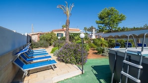 Área de piscina com espreguiçadeiras, uma palmeira e um céu azul límpido.