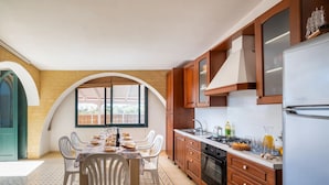 Cozinha com mesa de jantar posta para quatro, armários de madeira, geladeira e janela com vista para o quintal.