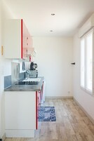 Cozinha moderna com armários brancos, parede de destaque vermelha, fogão embutido e janela que proporciona iluminação natural.