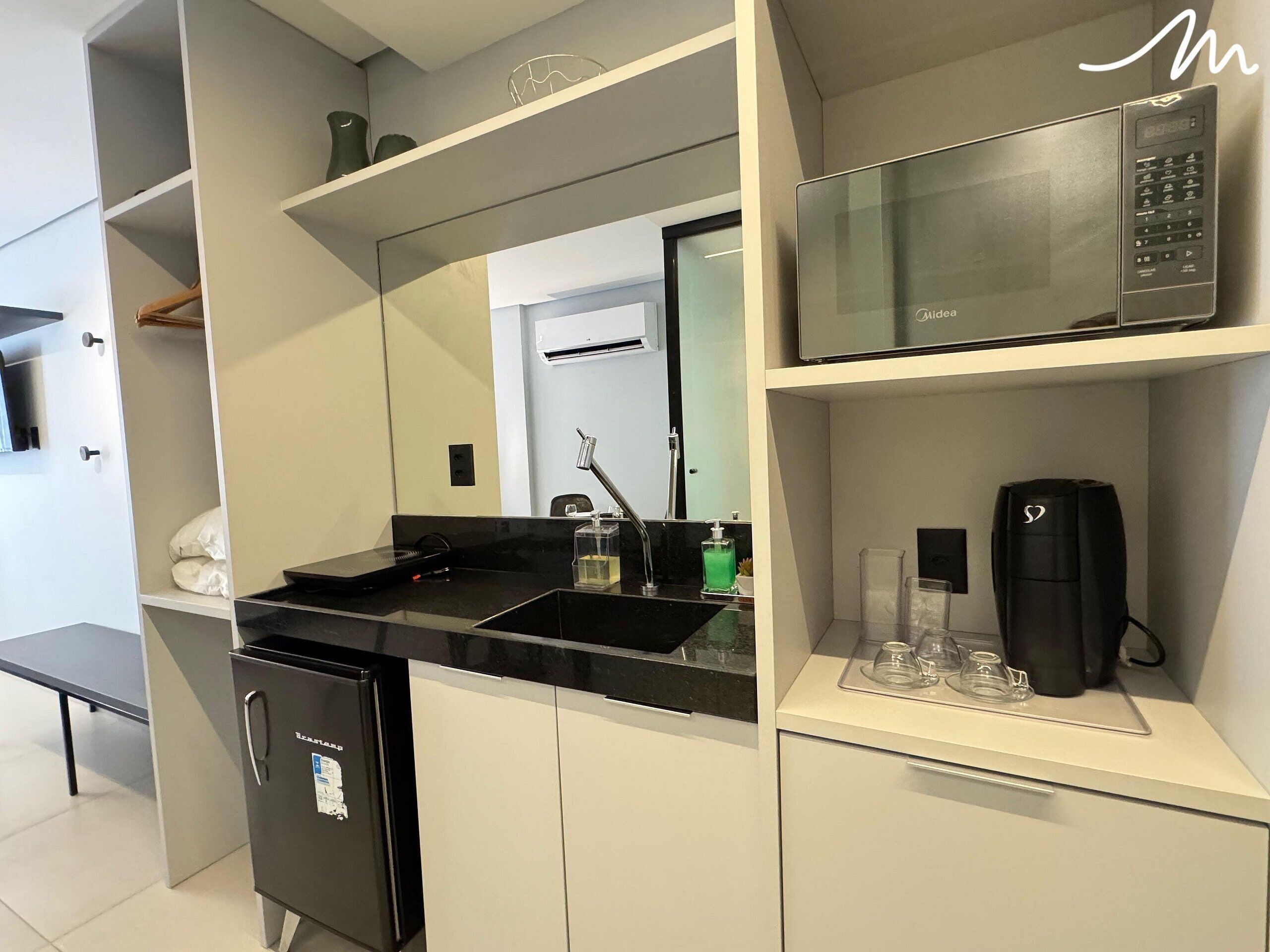 Uma cozinha compacta equipada com micro-ondas, cafeteira e geladeira.