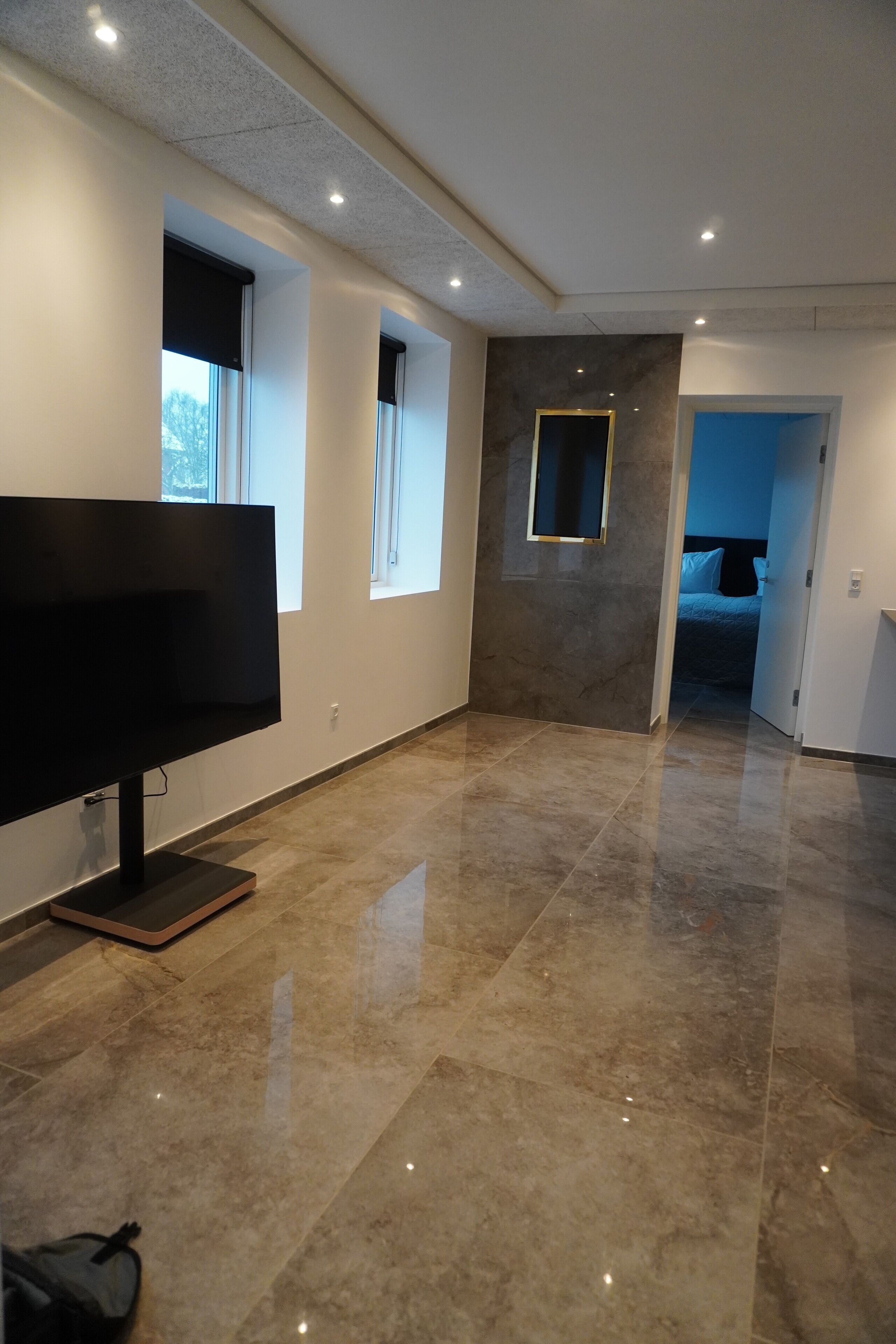 Uma sala de estar moderna com televisão de tela plana, grandes janelas e piso de mármore.