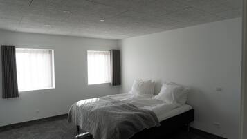 Quarto com cama, duas janelas com cortinas e chão de azulejos.