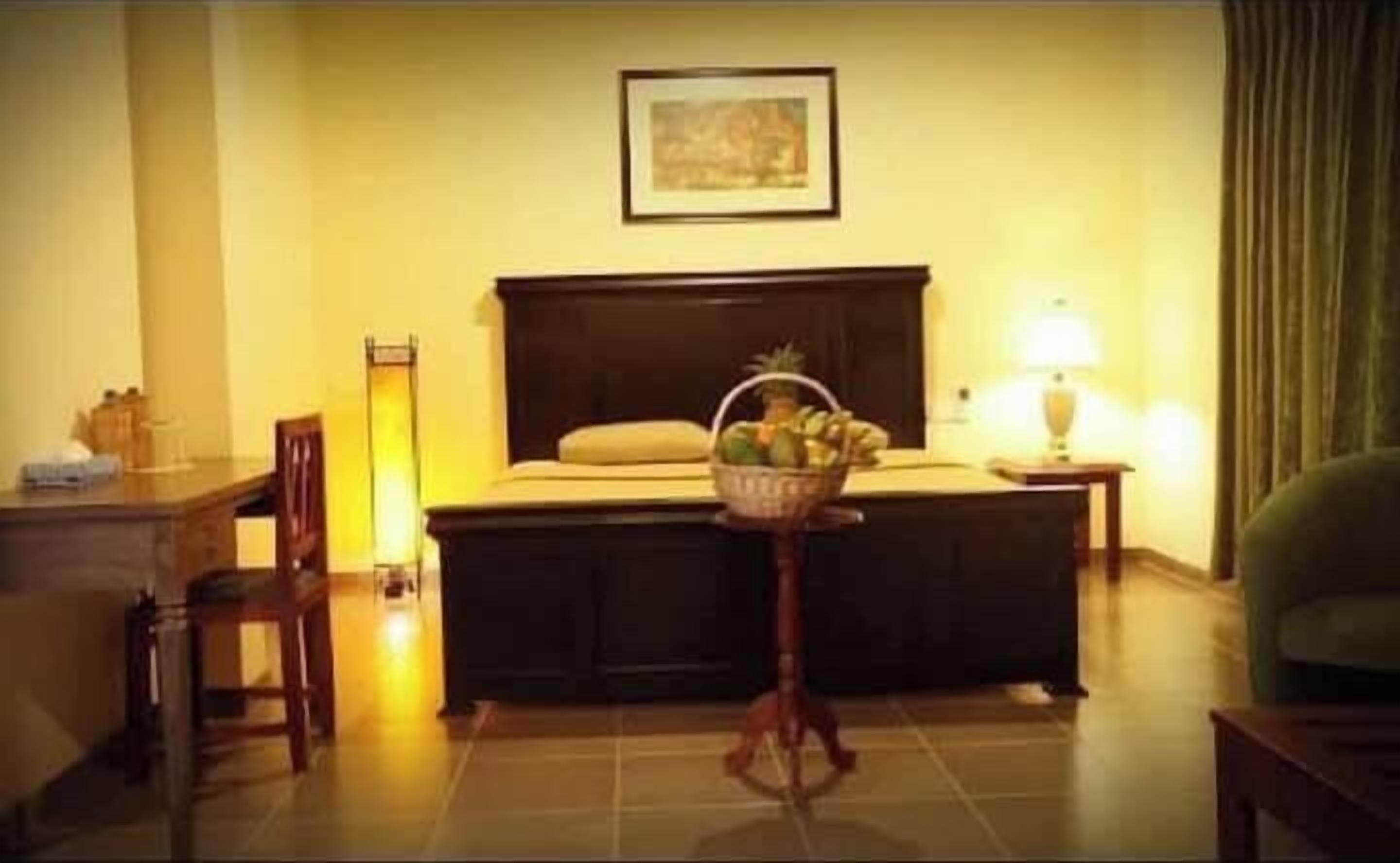 Quarto de hotel com uma cama, mesa de cabeceira, abajur, cadeira e um quadro pendurado na parede.