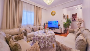 Uma sala de estar com sofás, televisão, lustre e objetos decorativos.