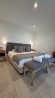 Quarto moderno com uma cama grande, mesas de cabeceira e um banquinho.