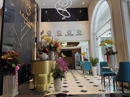 Um saguão de hotel com balcão de recepção, plantas em vasos grandes e um balcão de check-in.