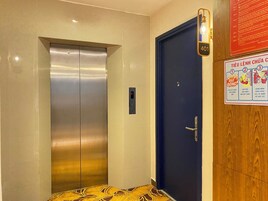Um elevador com painel digital, porta azul e cartaz de segurança contra incêndio na parede.