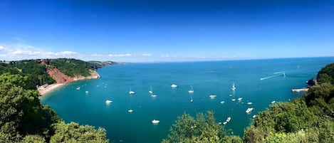 Vista costeira com barcos na água, uma praia e colinas verdes.