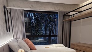 Quarto moderno com uma cama grande, mesa de cabeceira com abajur e vista para árvores pela janela.