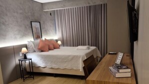 Quarto de hotel moderno com cama, mesa de cabeceira e escrivaninha com livros.
