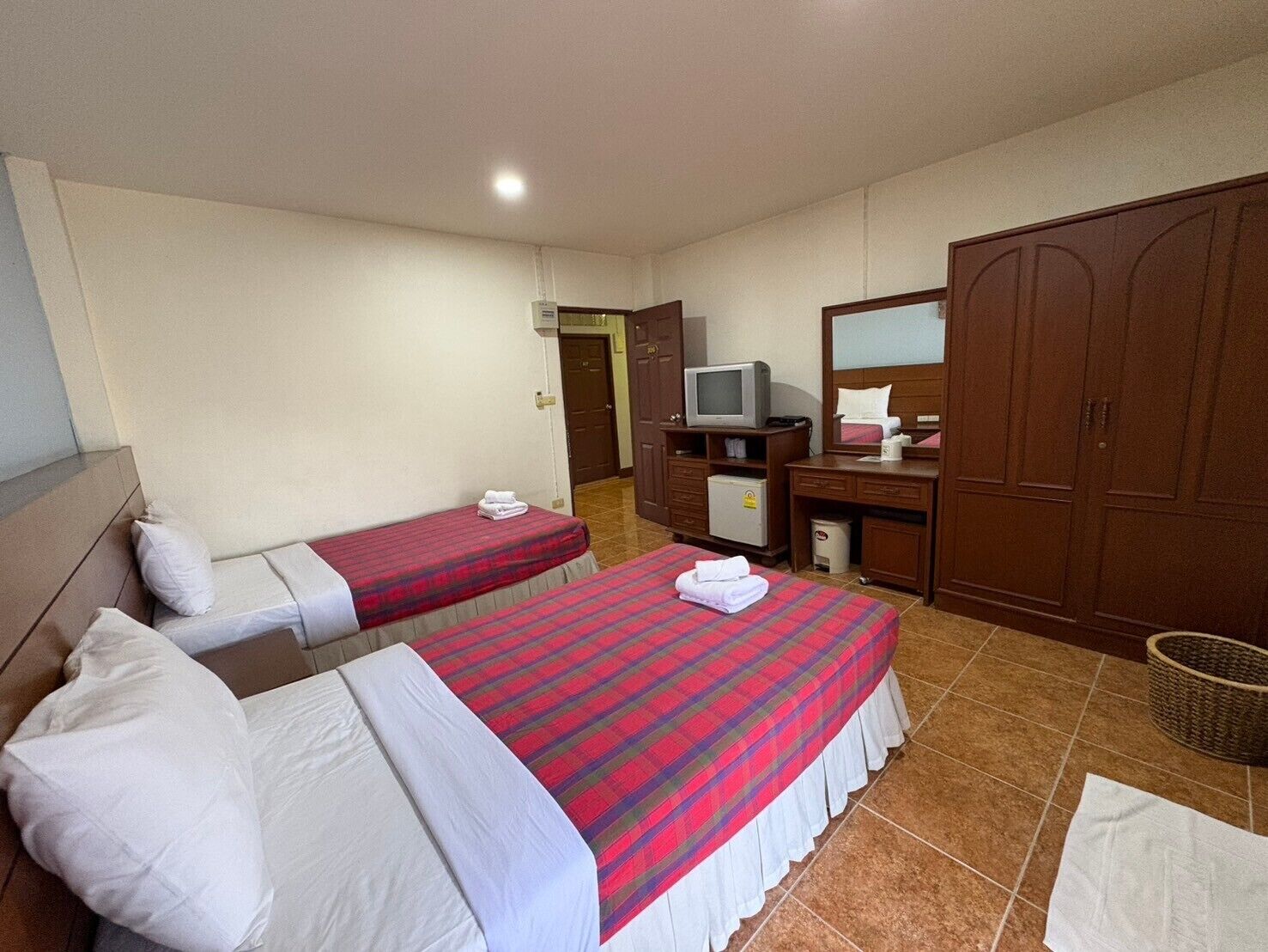 Quarto de hotel com duas camas, uma escrivaninha com televisão, um guarda-roupa e uma pequena lixeira.