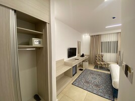Quarto de hotel moderno com guarda-roupa de madeira, televisão de tela plana, escrivaninha com cadeira, tapete estampado e janela com cortinas.