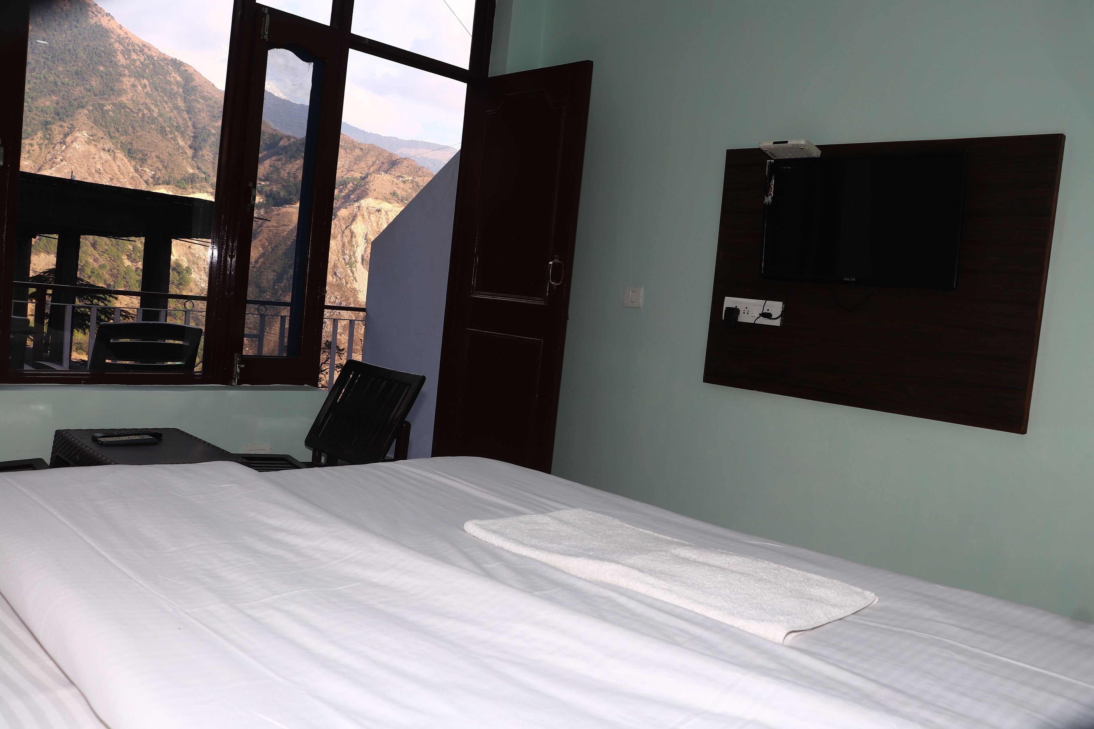 Quarto de hotel com uma cama, uma escrivaninha, uma cadeira, uma TV fixada na parede e uma janela com vista para as montanhas.