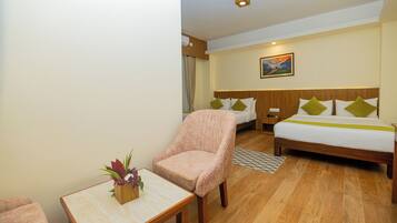 Quarto de hotel com cama, uma cadeira, uma pequena mesa com uma planta e um quadro na parede.