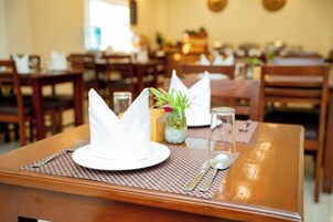 Uma mesa de jantar posta com uma toalha branca, um copo e um pequeno vaso com uma planta.